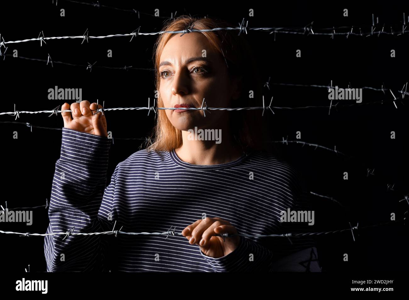 Mature Jewish woman behind barbed wire on black background ...