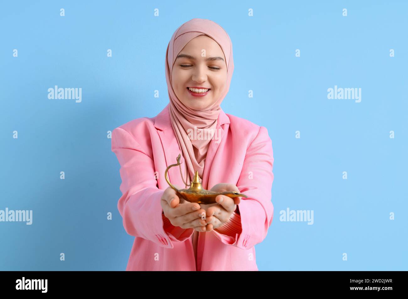 Young Muslim woman with Aladdin lamp on blue background. Ramadan ...