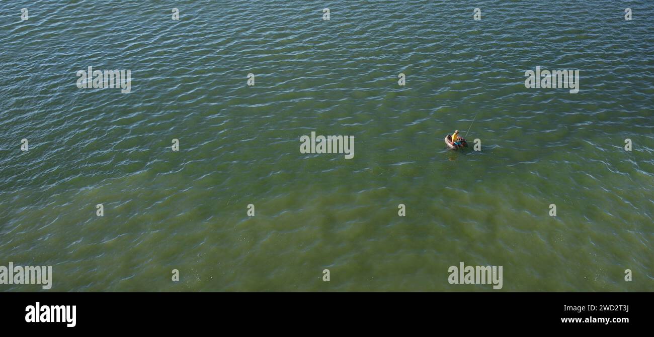 Float tube fisher floating over green waters of a reservoir. Long ...