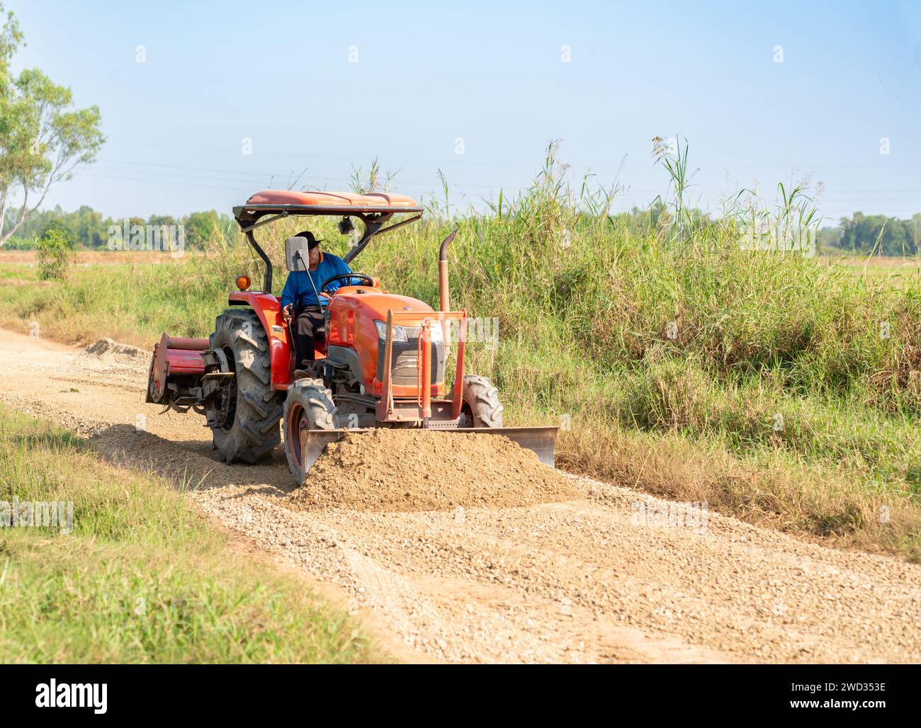 A stone-plowing tractor is leveling the road surface to enter the rice ...