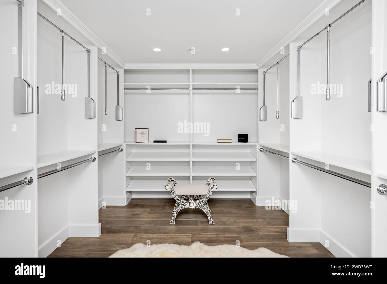 A contemporary, spacious white walk-in closet featuring organized ...