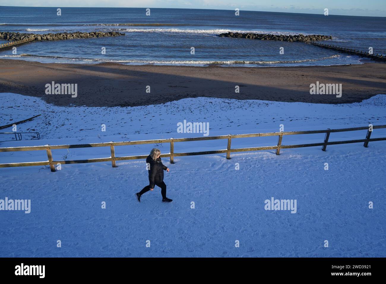 A person walks along a snow-covered beach front in Aberdeen. The UK ...