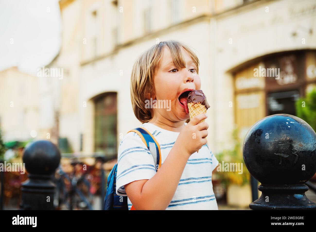 Cute little boy eating chocolate ice cream outdoors, wearing backpack ...