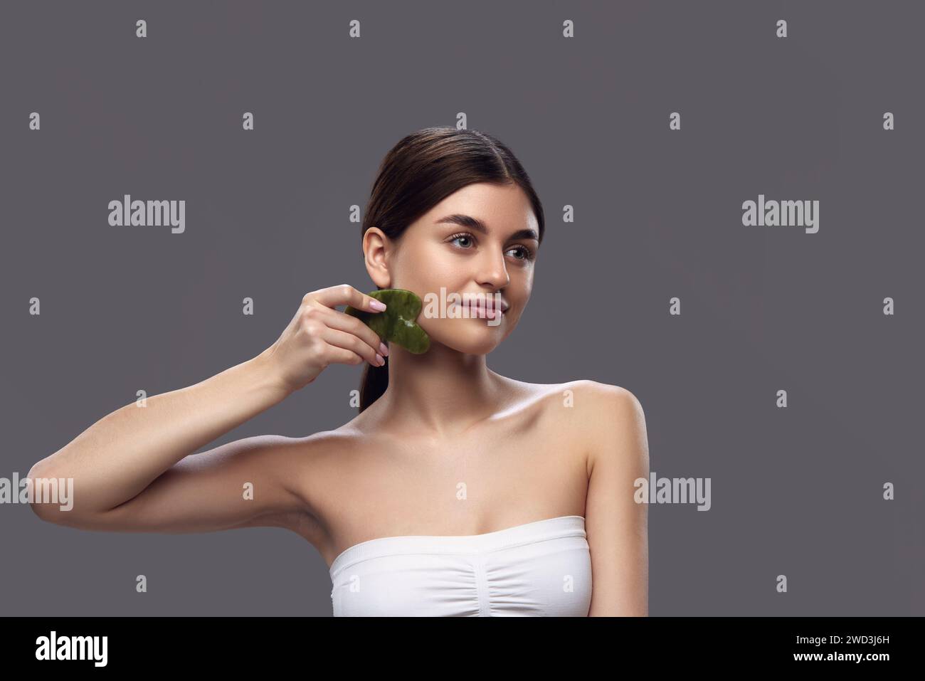 Portrait of young woman using green gua sha stone, portraying clean and ...
