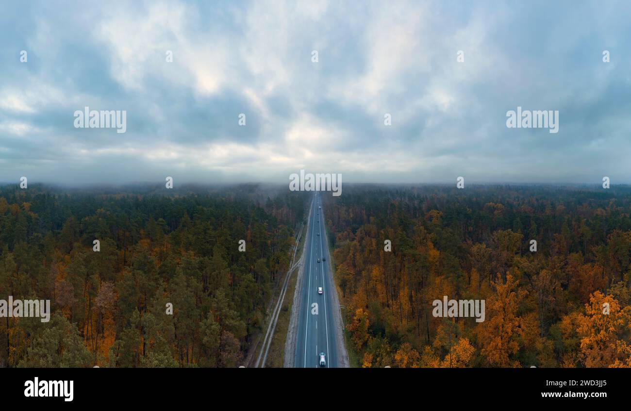 Highway road with passing cars in autumn forest with dark moody sky ...