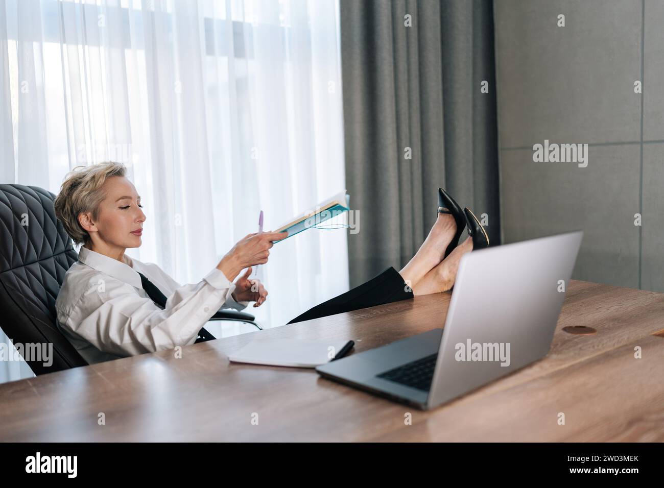 Relaxed middle-aged female CEO putting feet on desk with laptop ...