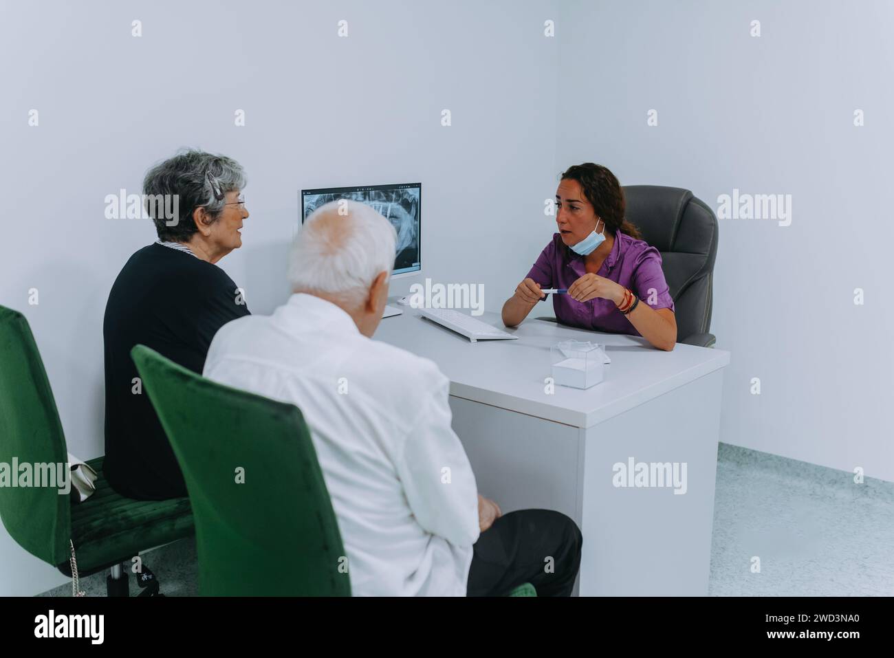 An elderly couple engages in a thoughtful discussion with their dentist ...
