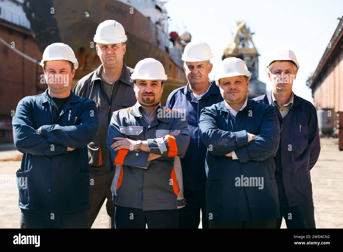 Shipyard workers at float dock wearing hard hats, stand arms-crossed ...
