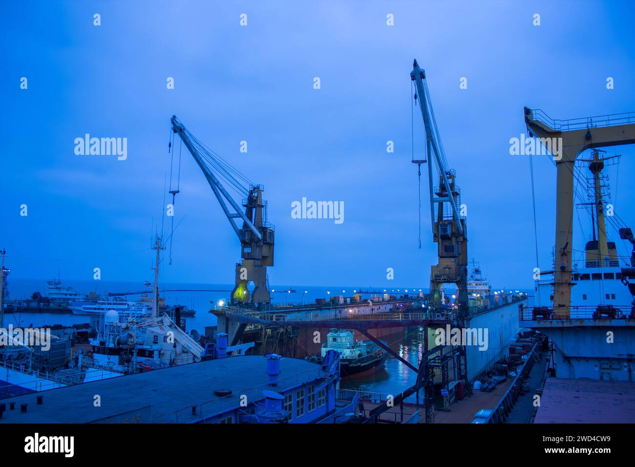 Industrial shipyard at dusk, floating dry dock with ship under repair ...