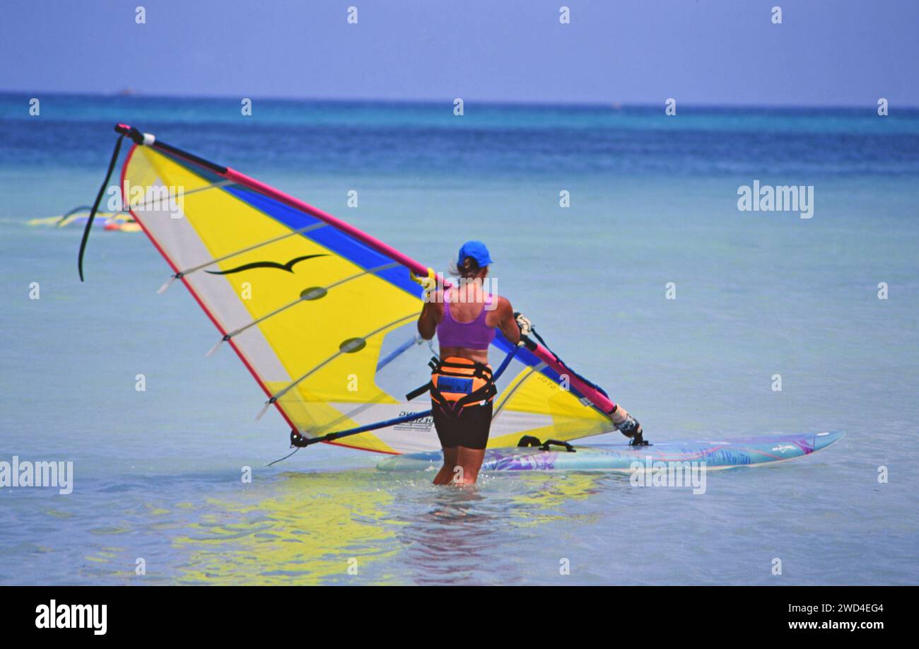 A young woman windsurfing student learning to rig her board in the ...