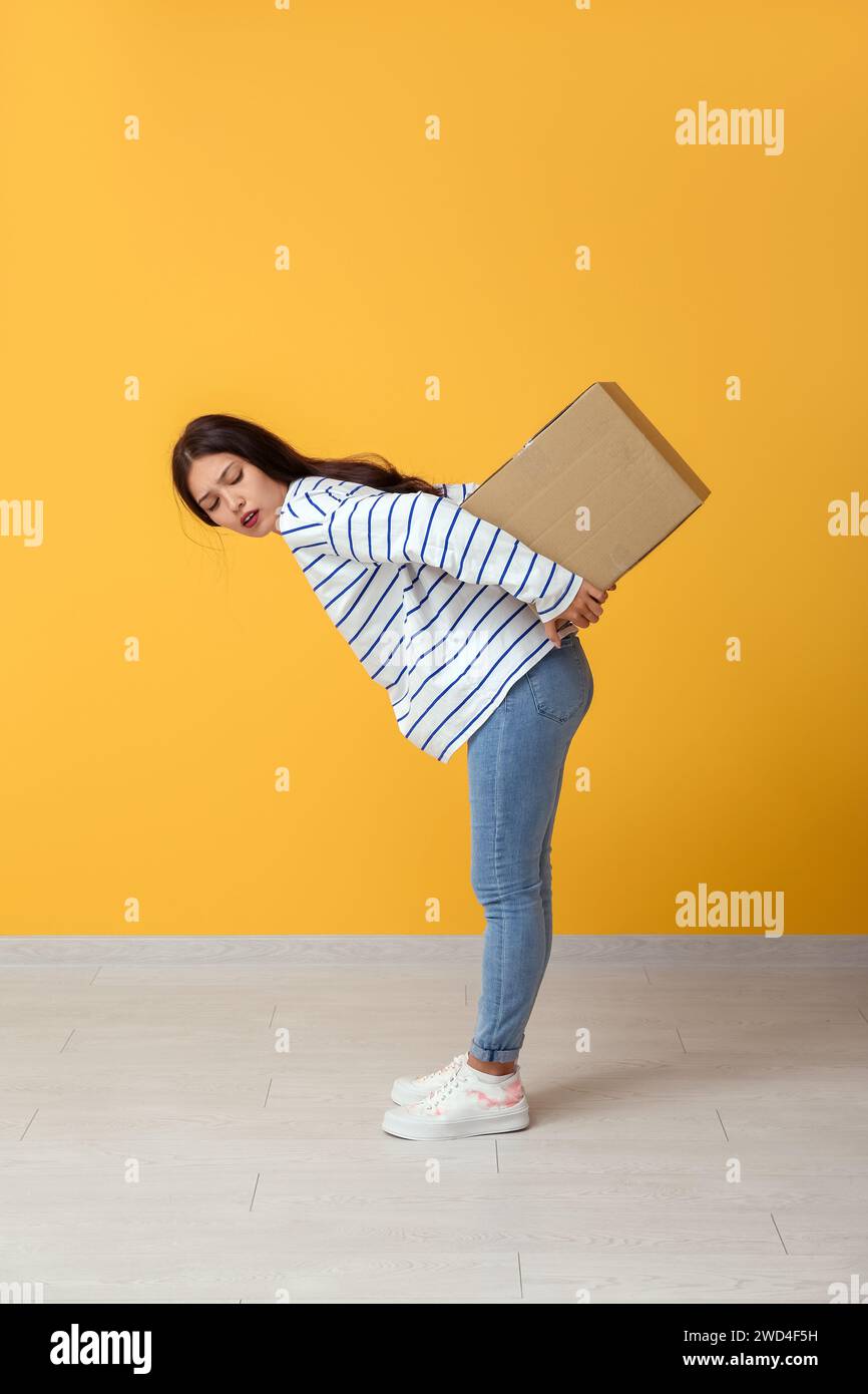 Pretty young woman carrying heavy parcel on her back against yellow ...