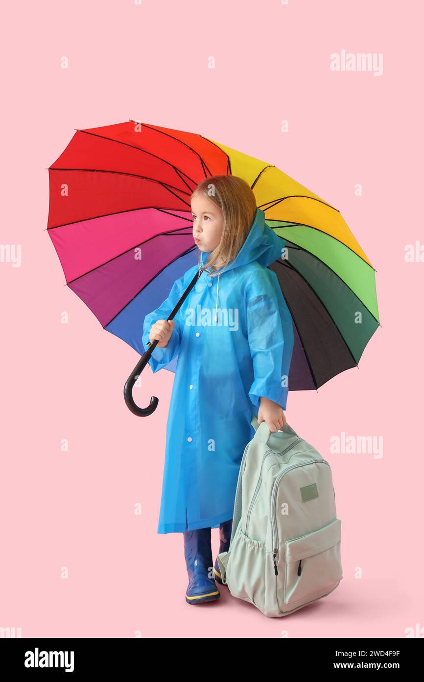Cute little schoolgirl in raincoat with backpack and umbrella walking on pink background Stock ...