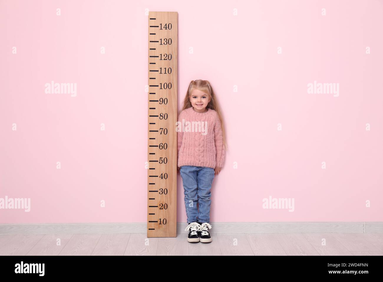 Cute little girl measuring height near pink wall Stock Photo - Alamy