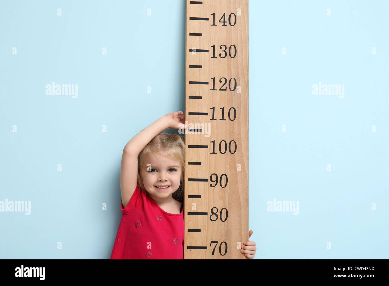 Cute little girl measuring height on blue background Stock Photo - Alamy
