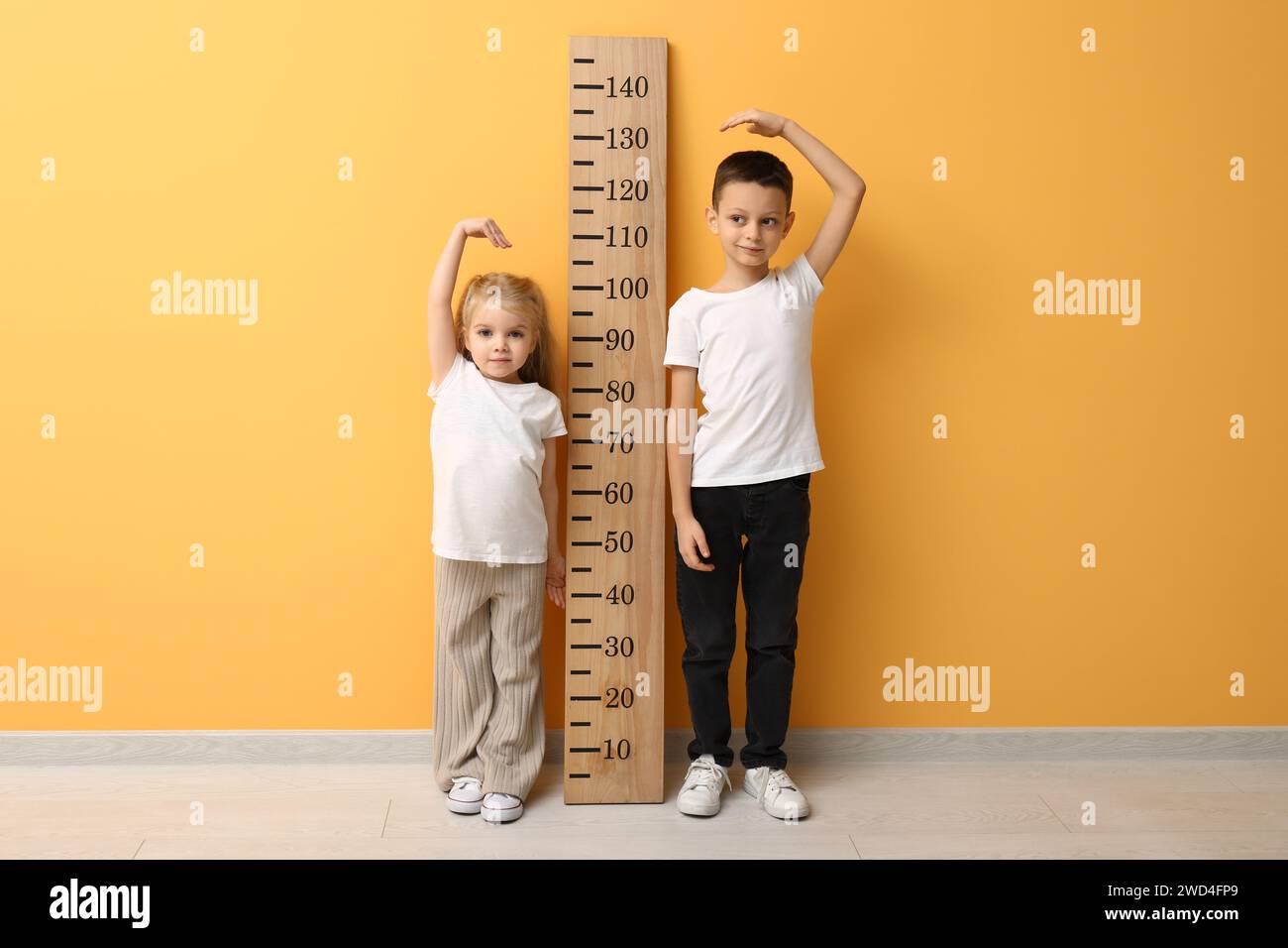 Cute little children measuring height near yellow wall Stock Photo - Alamy