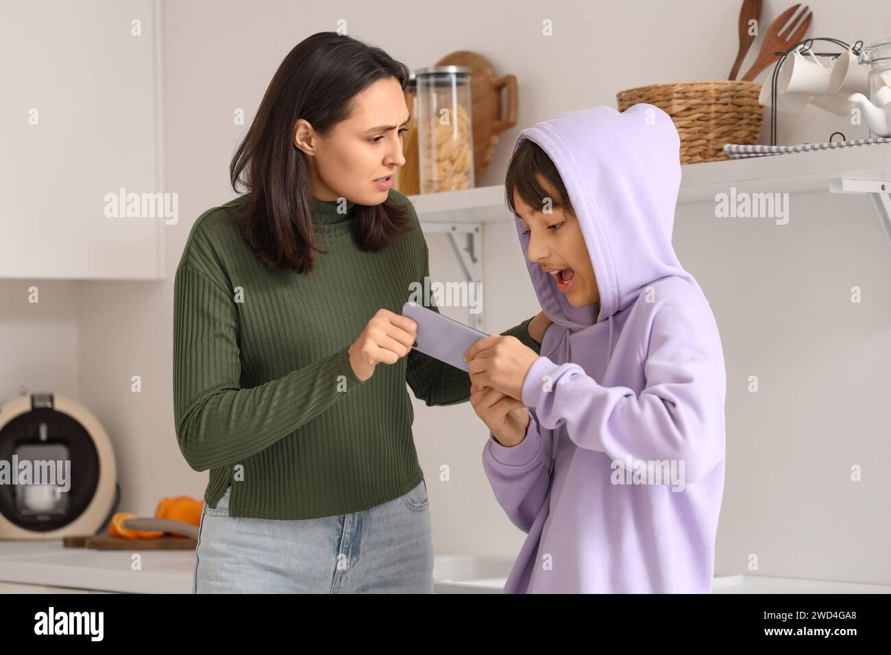 Angry mother taking mobile phone away from her teenage son in kitchen ...