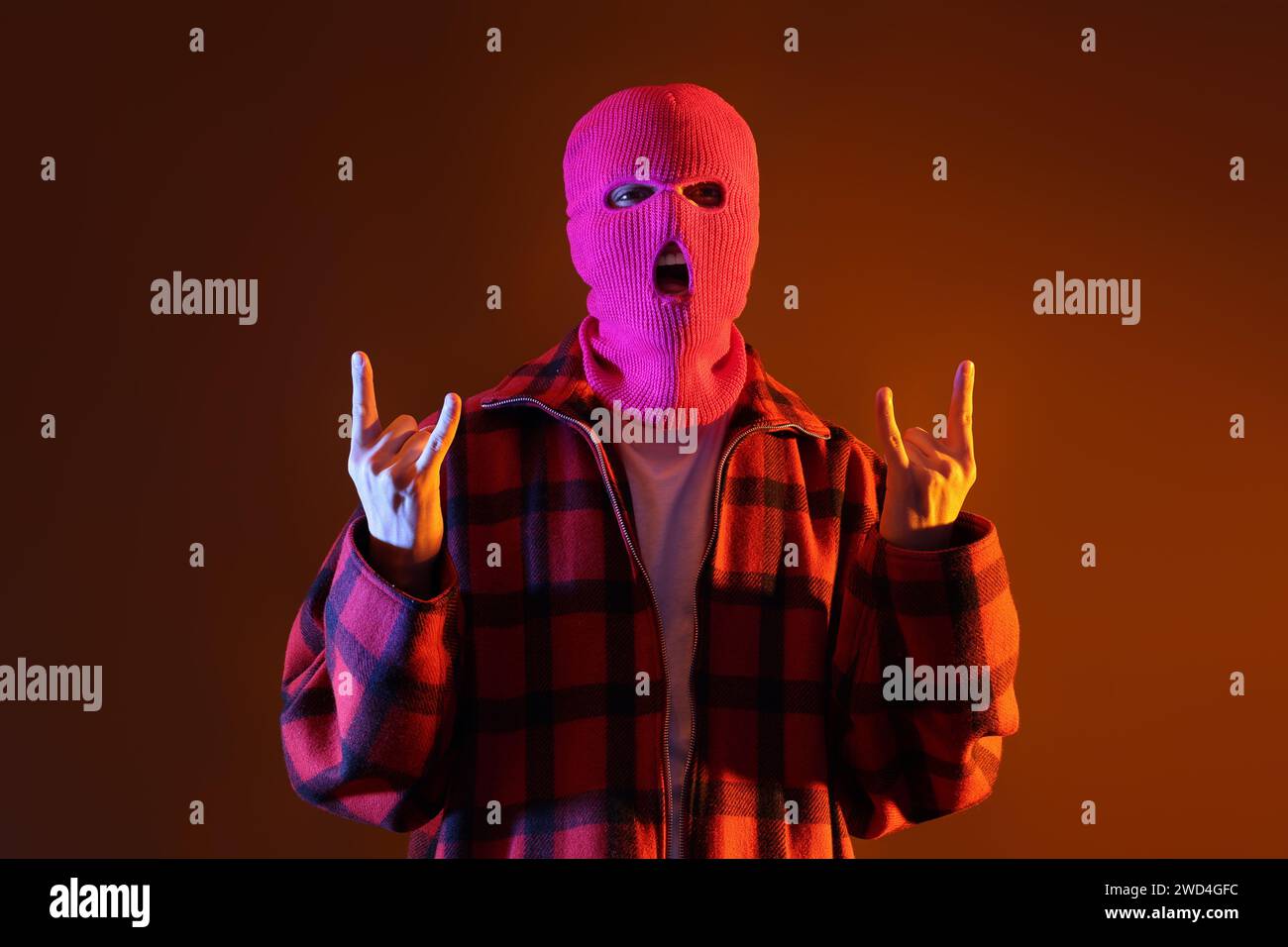 Handsome young man in balaclava showing "devil horns" gesture on black ...