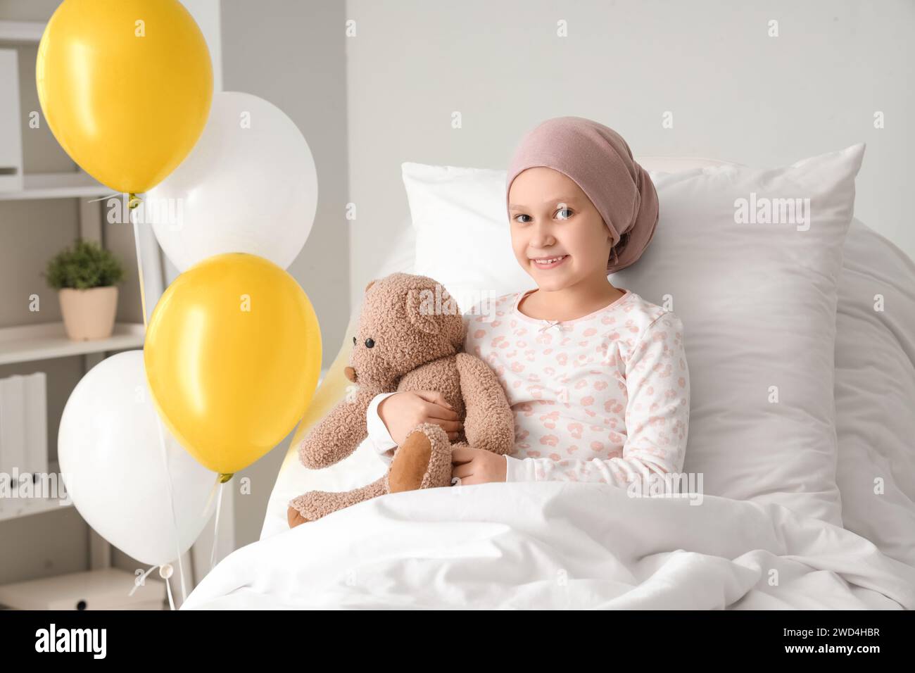 Little girl after chemotherapy with toy bear lying in bed at hospital ...