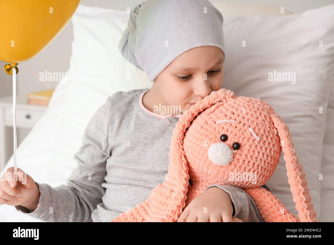 Little girl after chemotherapy with blue balloon and toy lying in ...