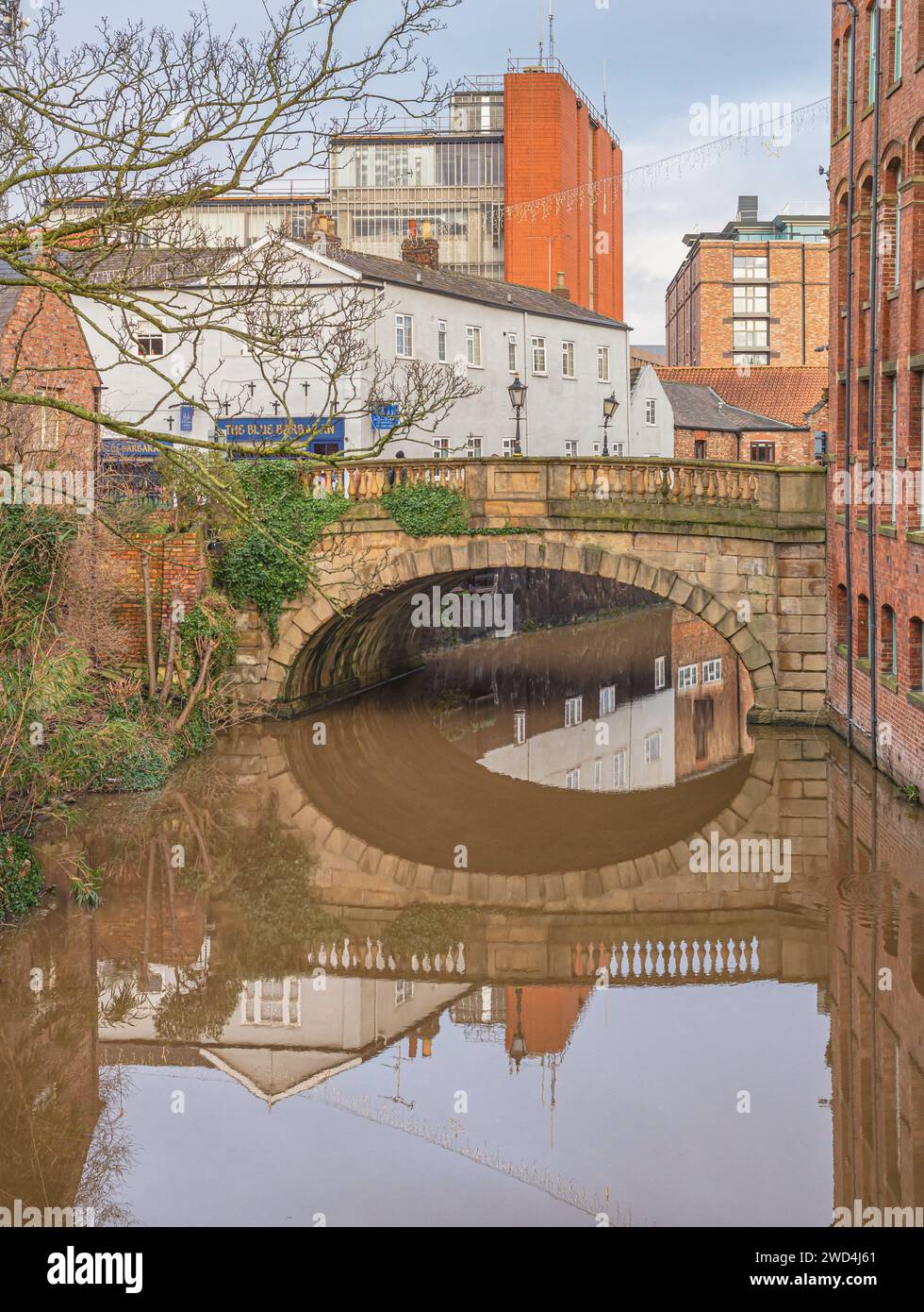 A river flows under an ancient stone bridge which is reflected in the ...