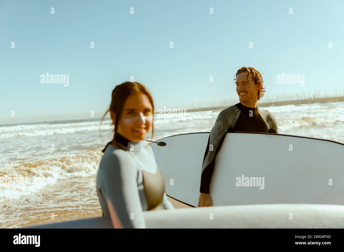 Two happy surfers in wetsuit with his surfboards entering out of sea ...