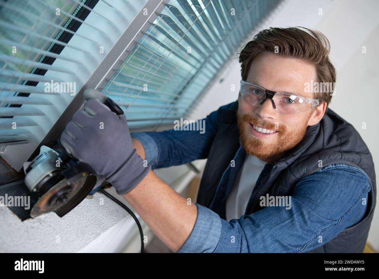 man fixing metal frame using angle grinder on windows Stock Photo - Alamy