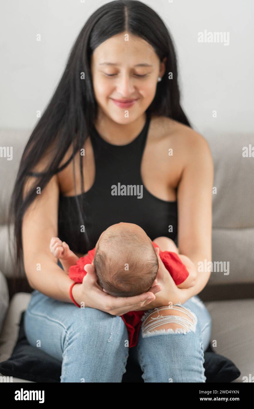 young latina mother carrying her baby on her lap while looking at her ...