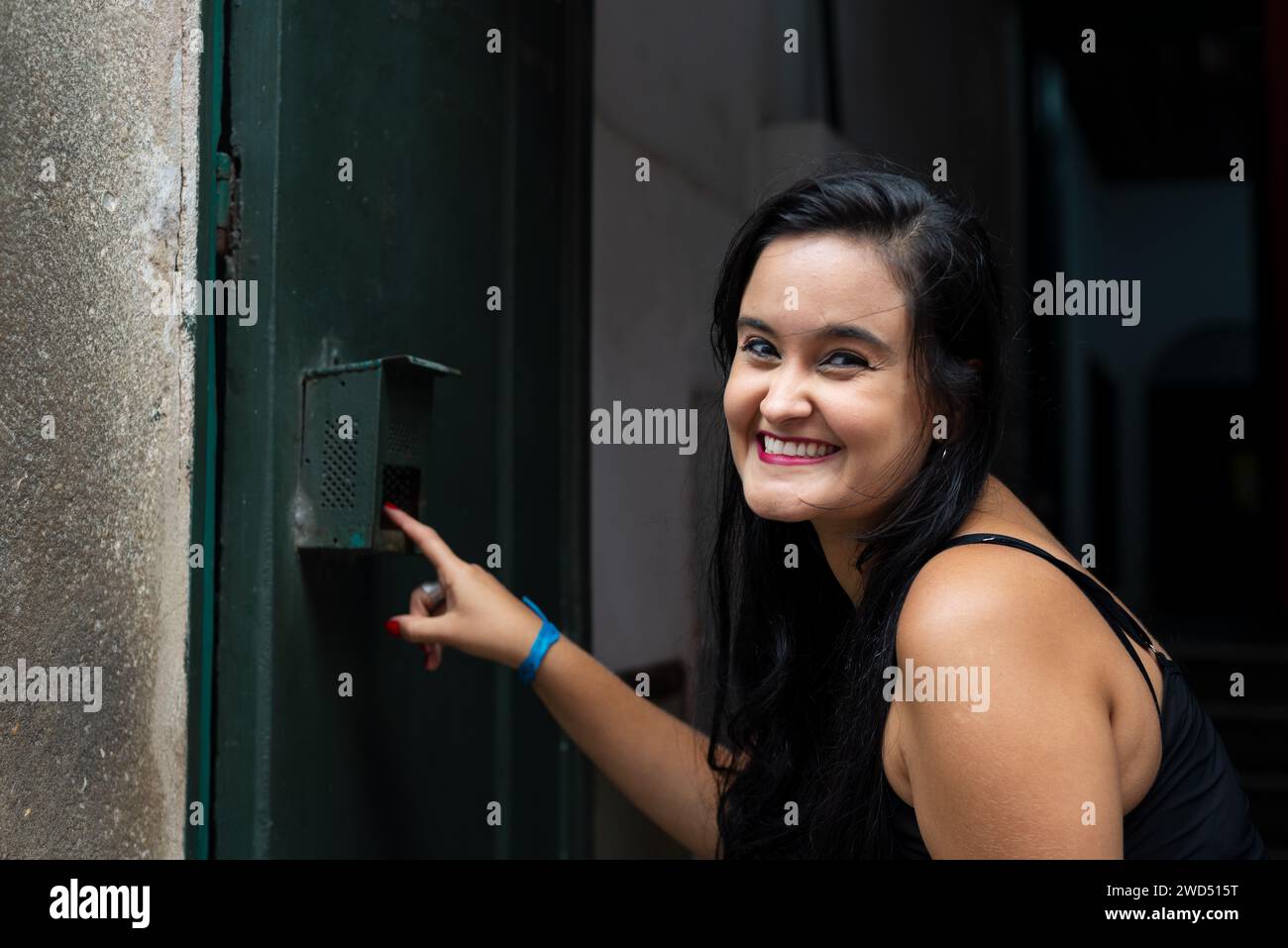 Portrait of beautiful young woman with black hair ringing the doorbell ...
