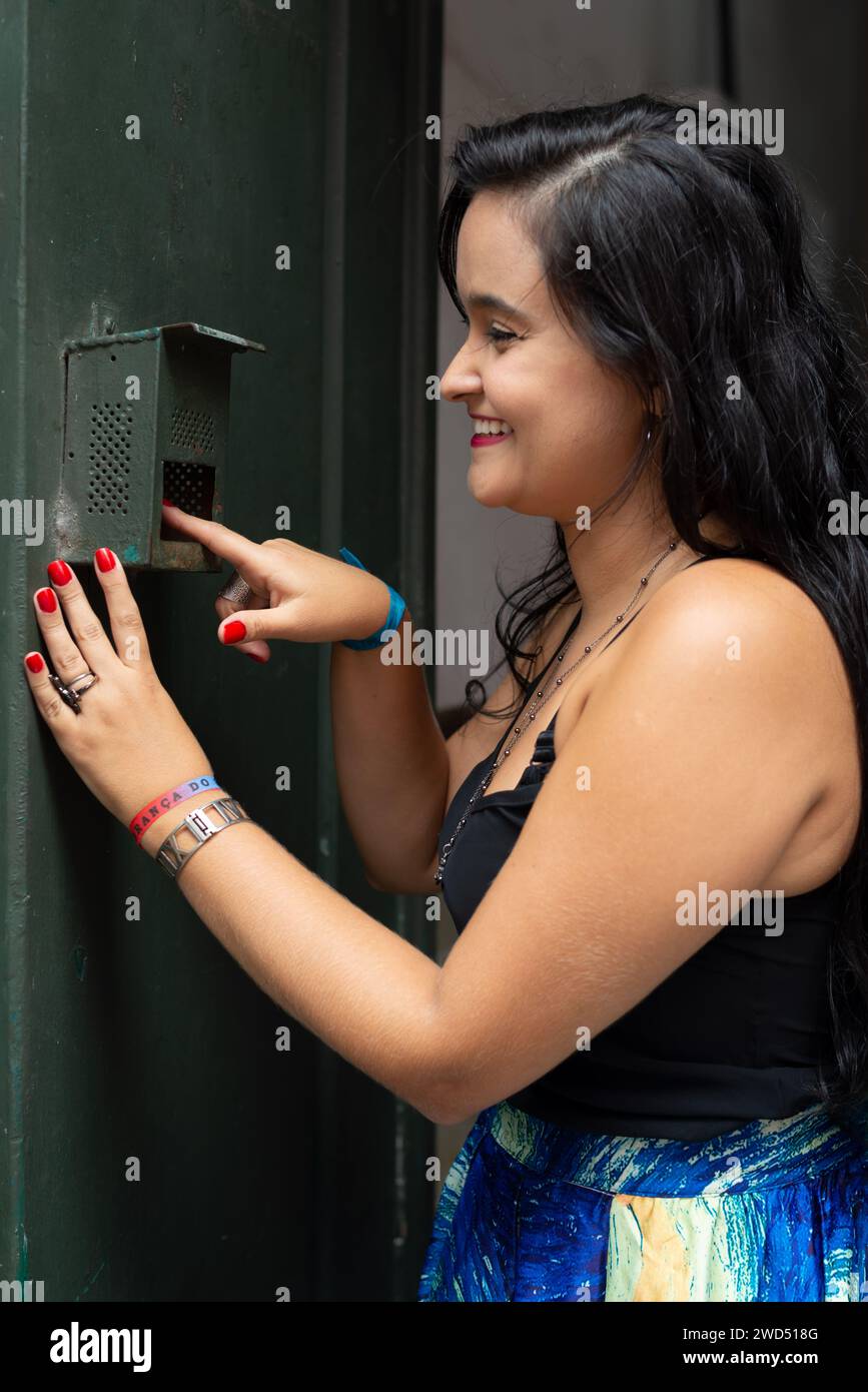 Portrait of beautiful young woman with black hair ringing the doorbell ...