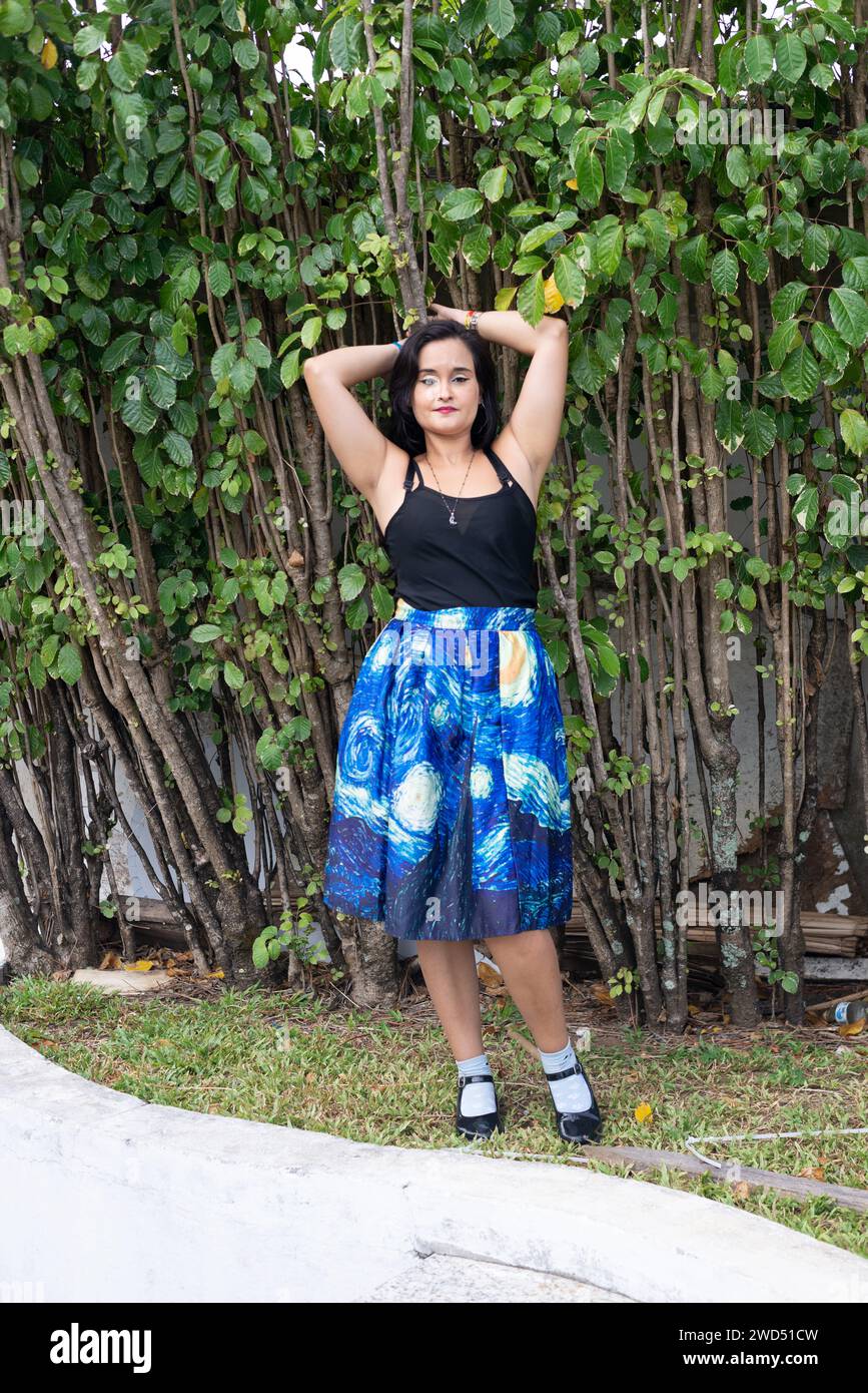 Beautiful young woman, with long black hair, leaning against a green ...