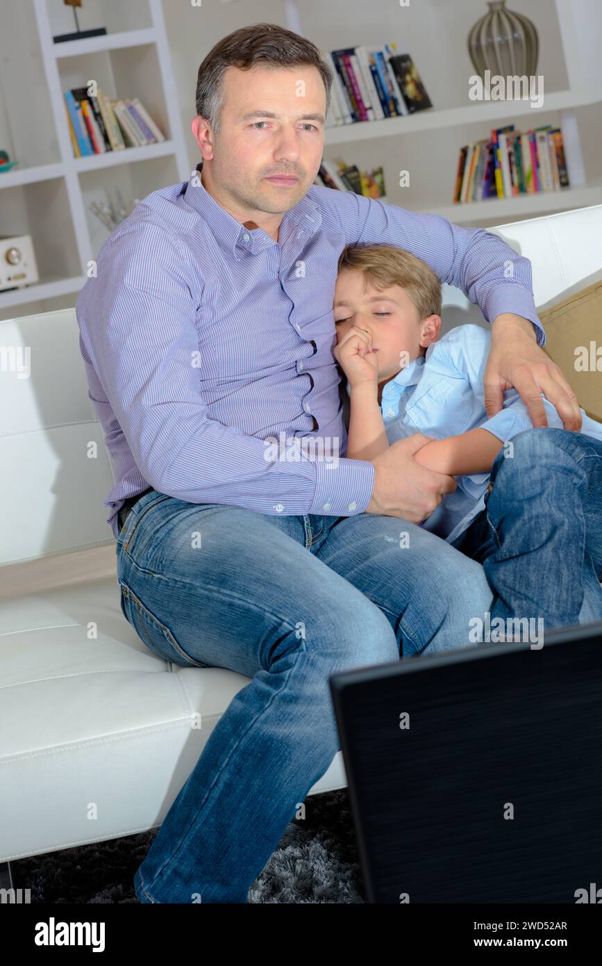 Man watching television, child fallen asleep beside him Stock Photo - Alamy