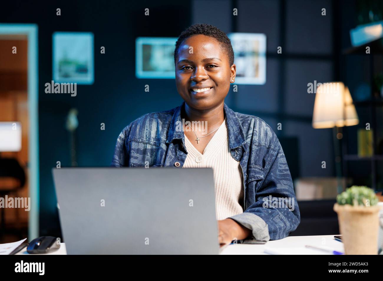 Black woman working at her laptop in a modern apartment, studying online and researching ...