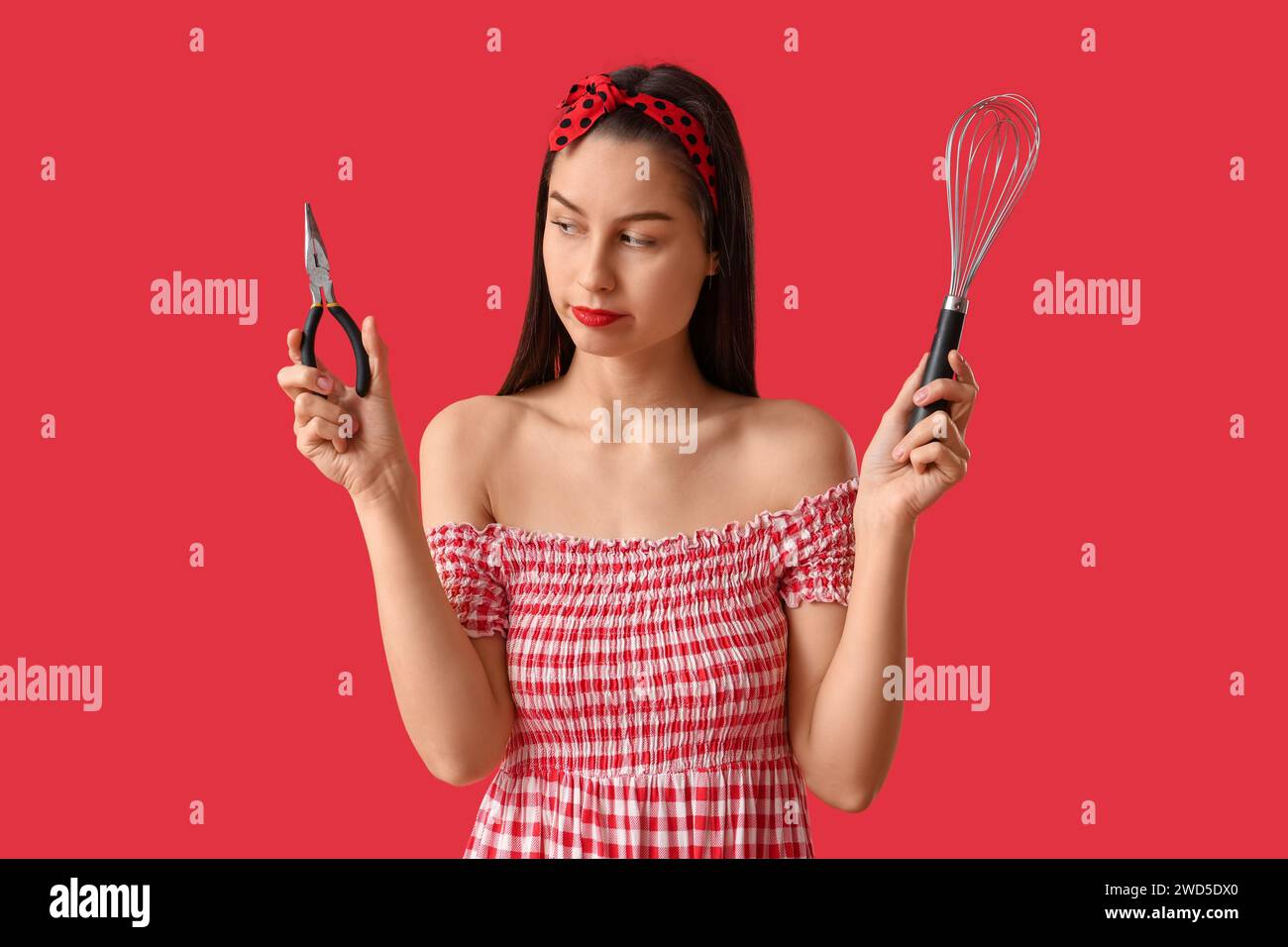 Portrait of young pin-up woman with whisk and pliers on red background ...