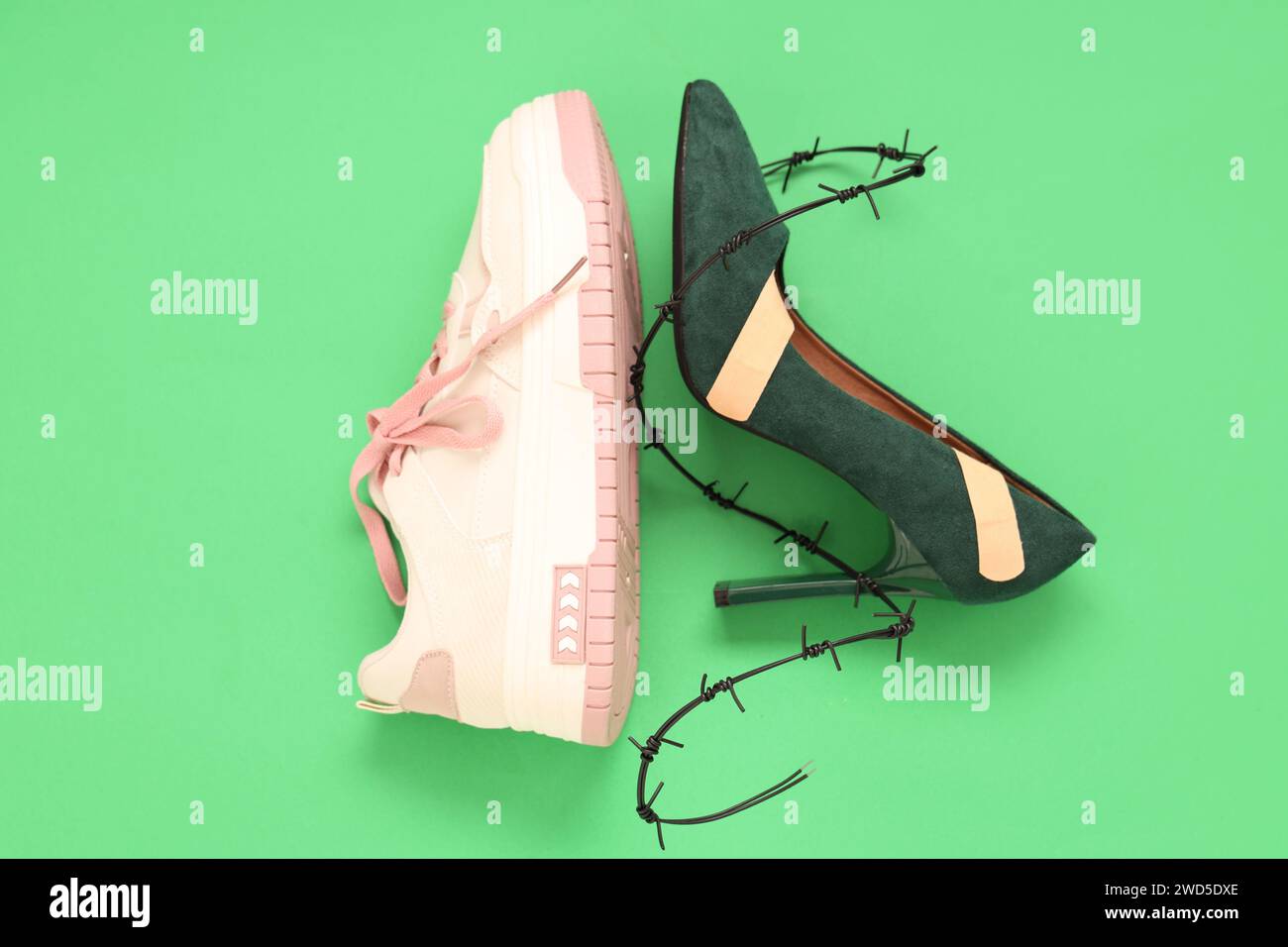 Sneaker and high-heeled shoe wrapped in barbed wire on green background ...