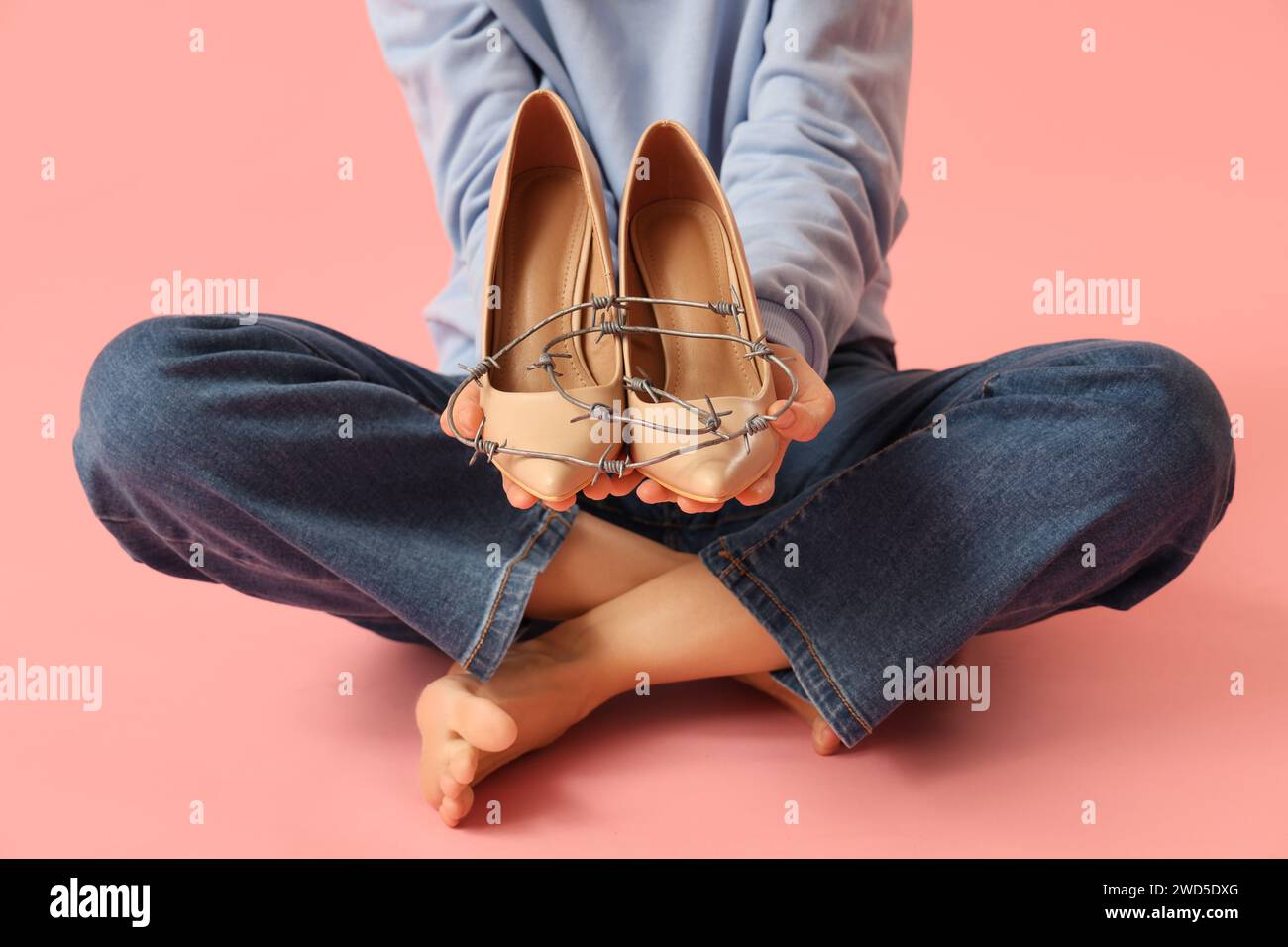 Young woman holding shoes in barbed wire on pink background ...