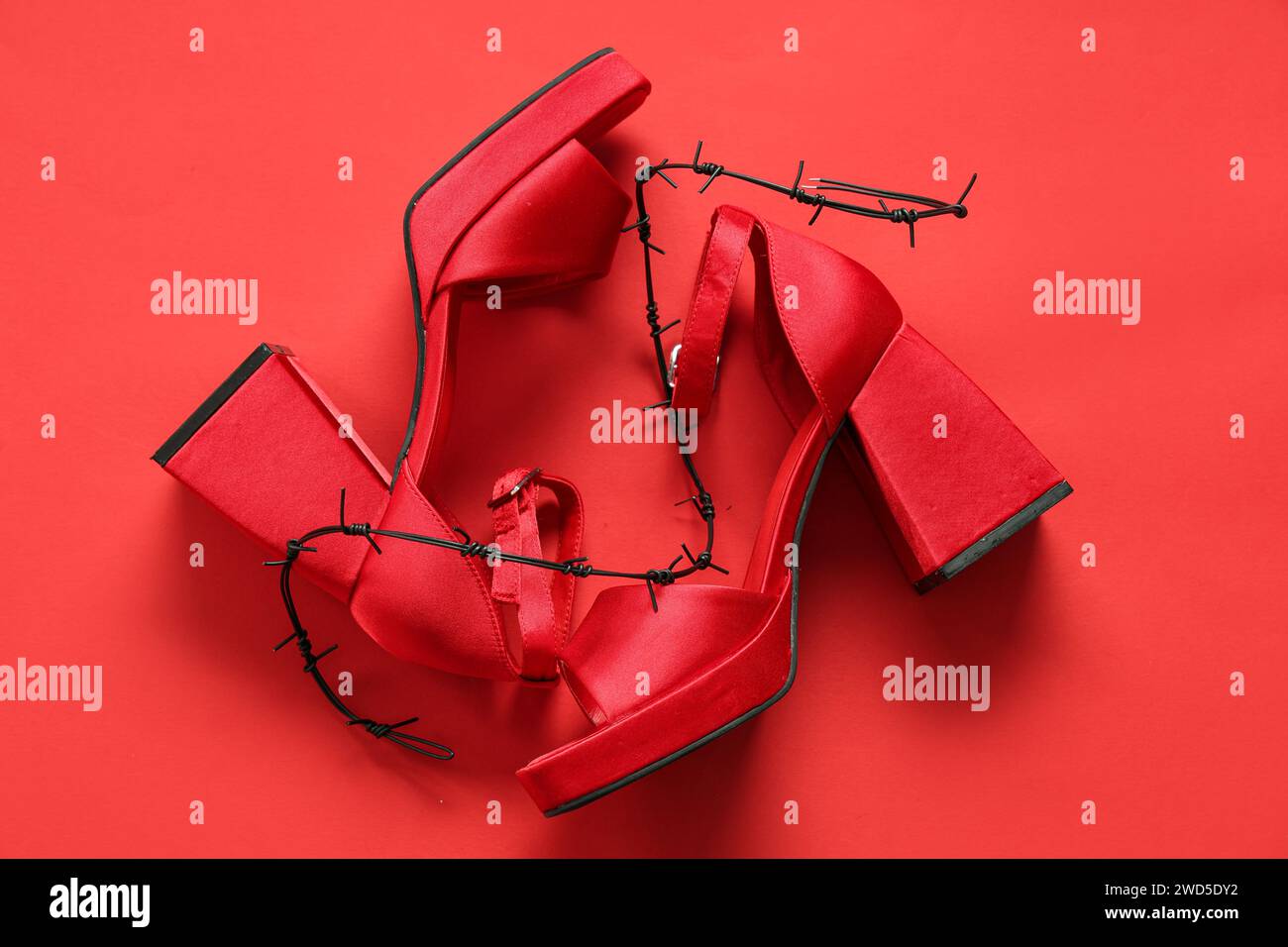 High-heeled shoes wrapped in barbed wire on red background ...