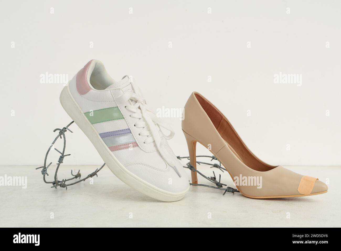 High-heeled shoe wrapped in barbed wire and sneaker on white background ...