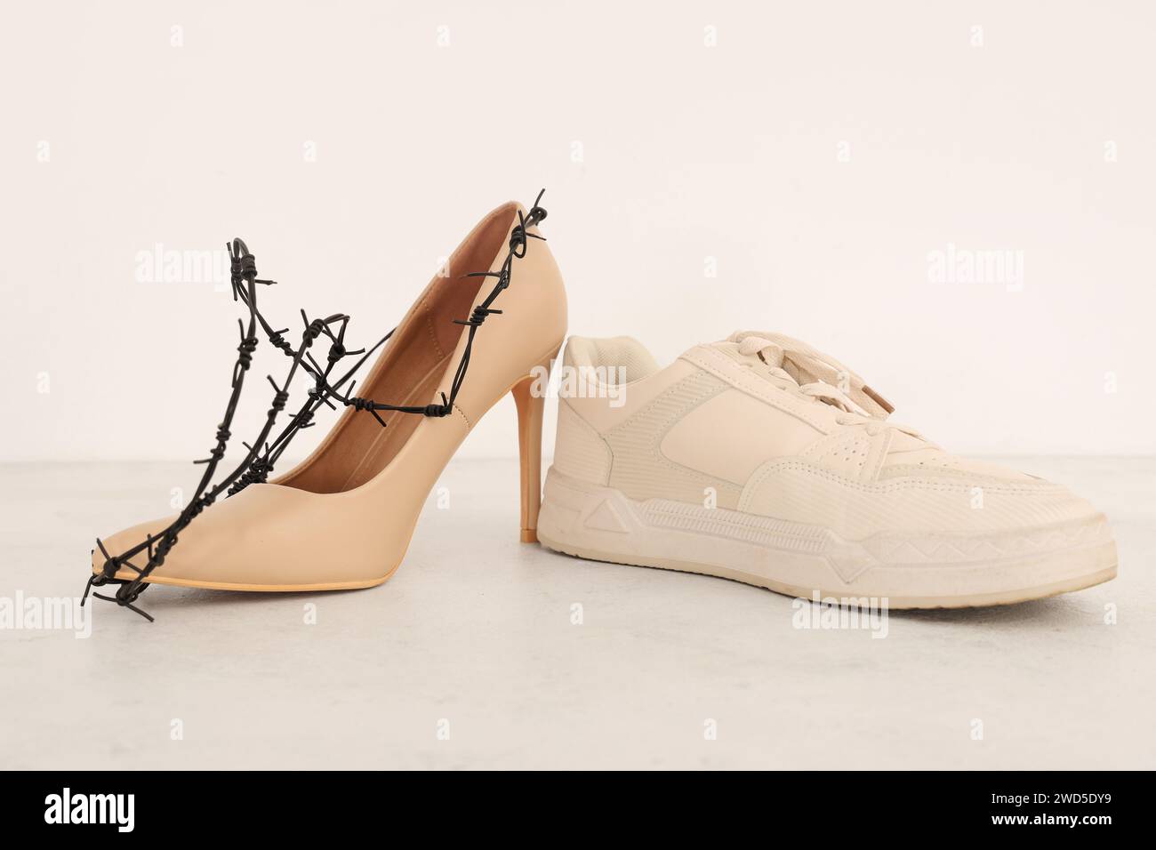 High-heeled sneaker and shoe wrapped in barbed wire on white background ...