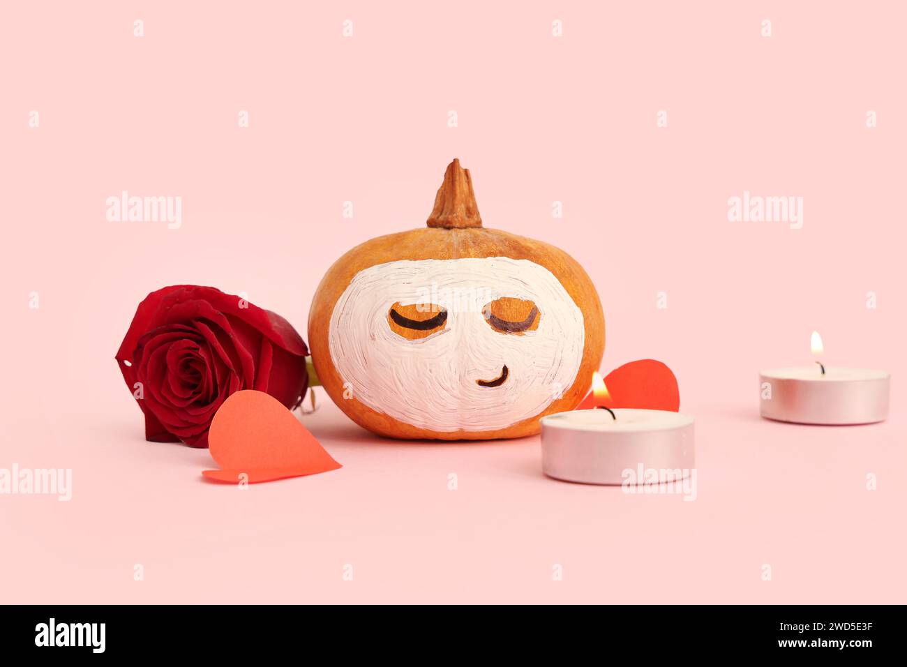 Pumpkin with drawn face, candles, paper hearts and clay mask on pink ...