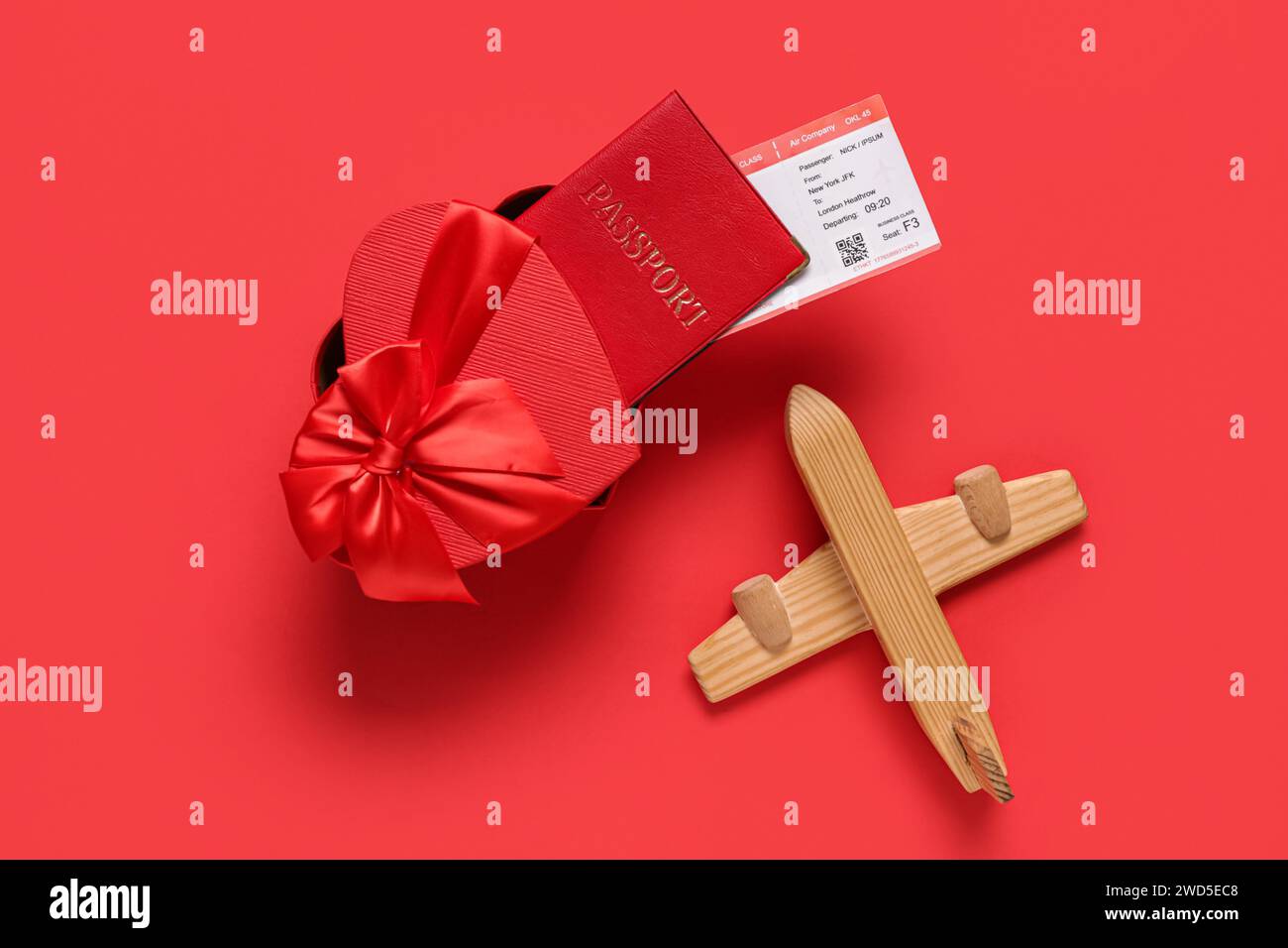 Gift box with passport, ticket and wooden airplane on red background ...