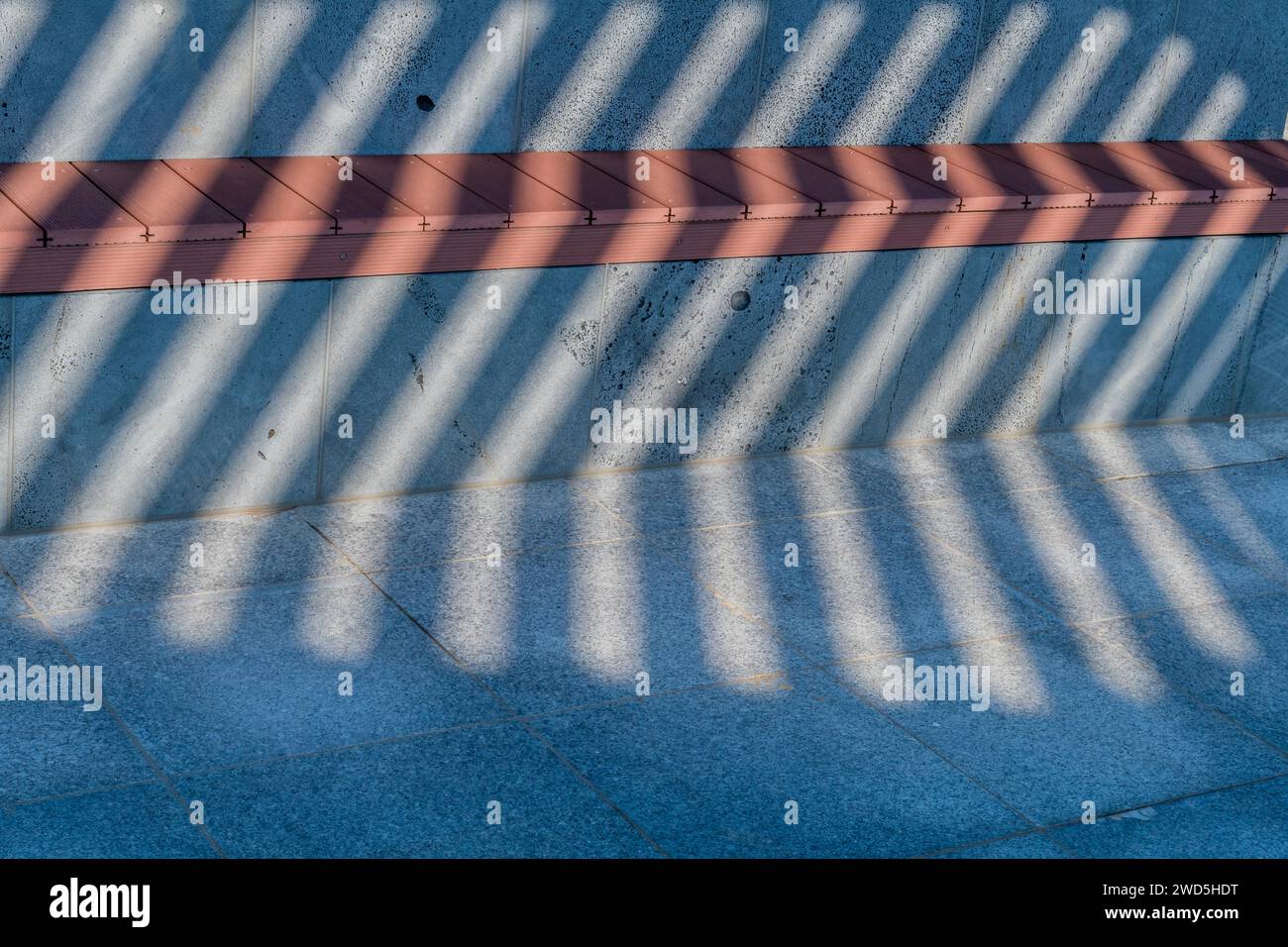 Striped pattern caused by shadows on concrete and wooden bench in local ...