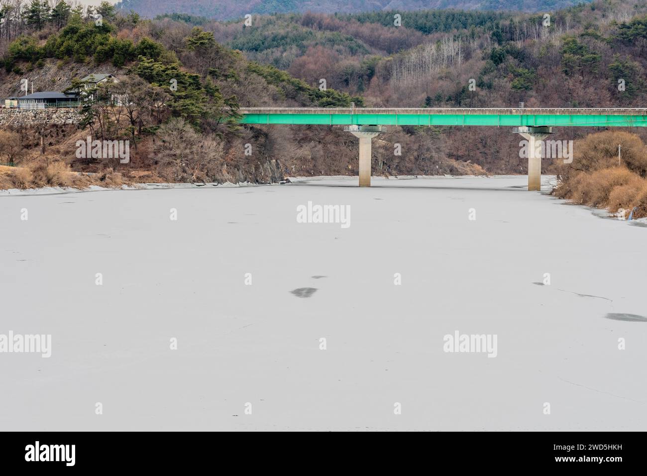 Green bridge over frozen river in mountain valley with mountains in ...