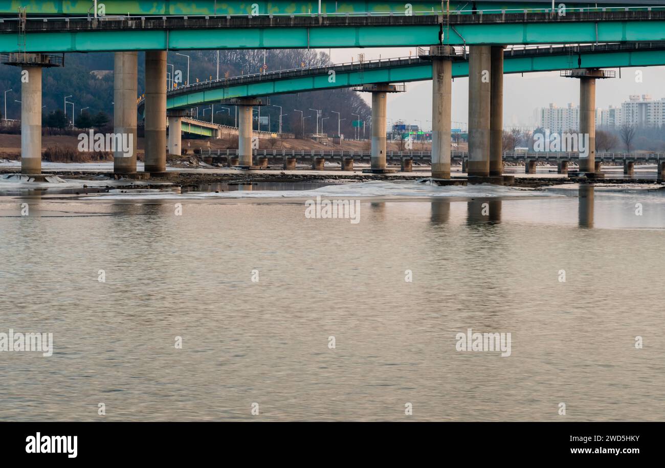 Bridges over partially frozen river with city buildings and trees in ...