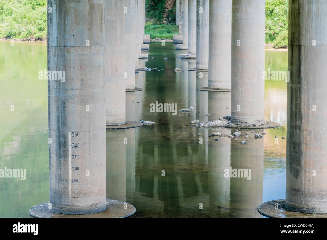 Concrete columns of bridge across reflecting in water of shallow river ...