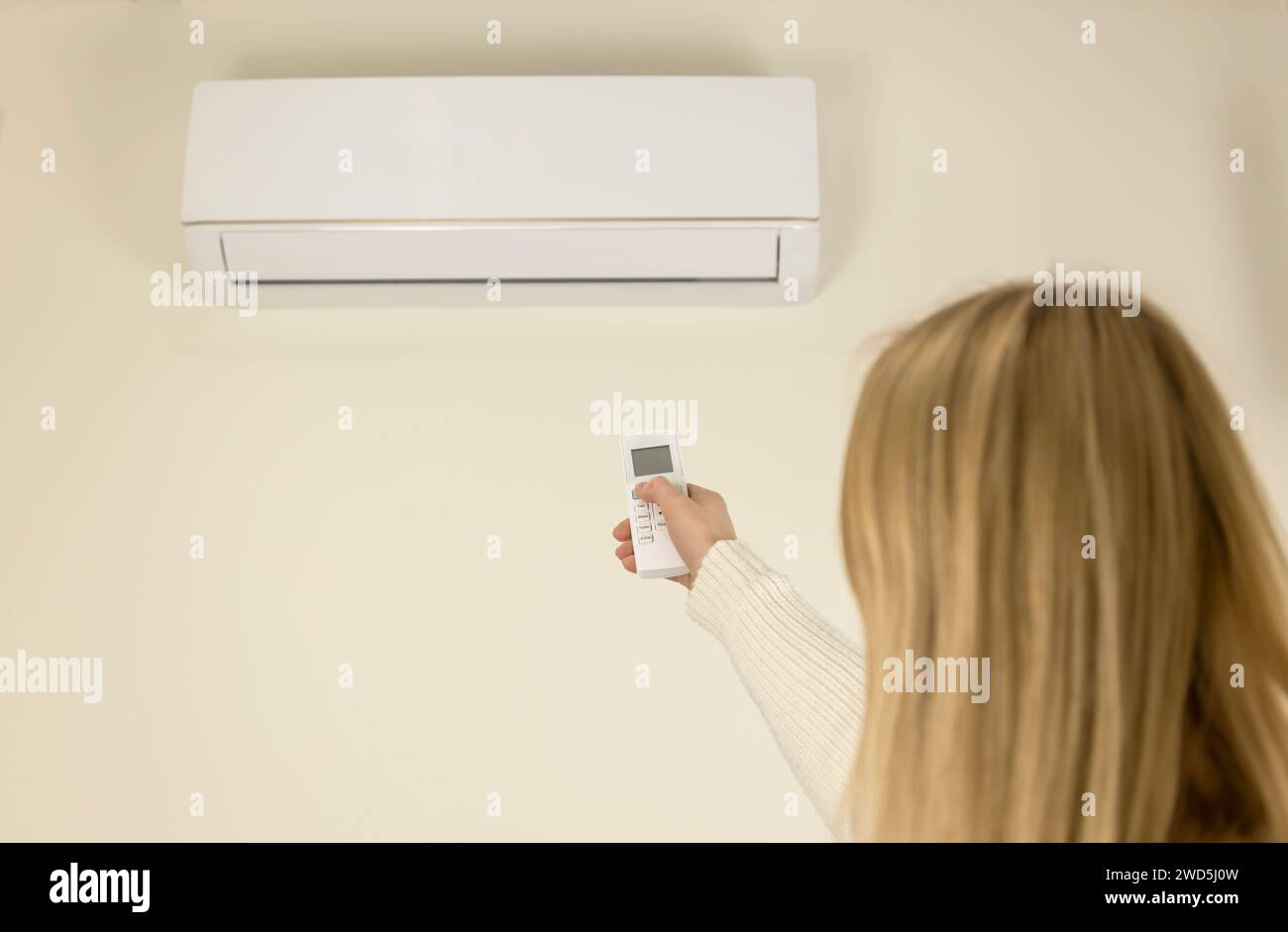 Back view of a woman controlling the air temperature in the house with ...