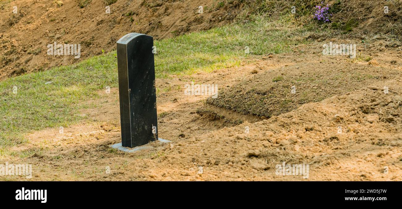 Newly dug grave mound with granite marker in wooded area on mountain in ...