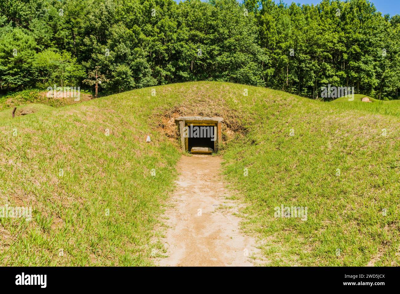 Unmarked mound tomb with dirt path leading to concrete opening on dry ...