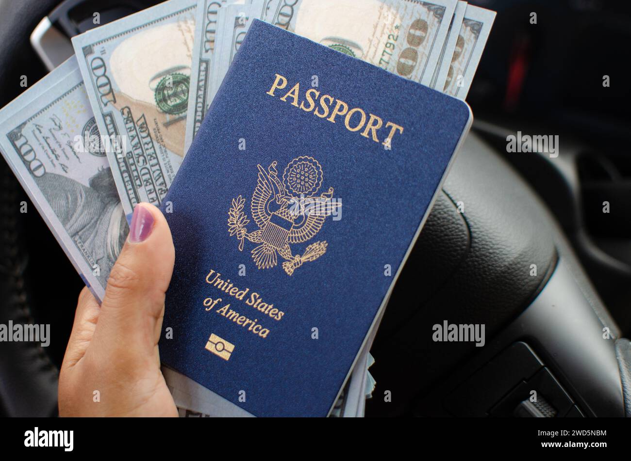 Inside a car, a hand holds a closed American passport, revealing the ...