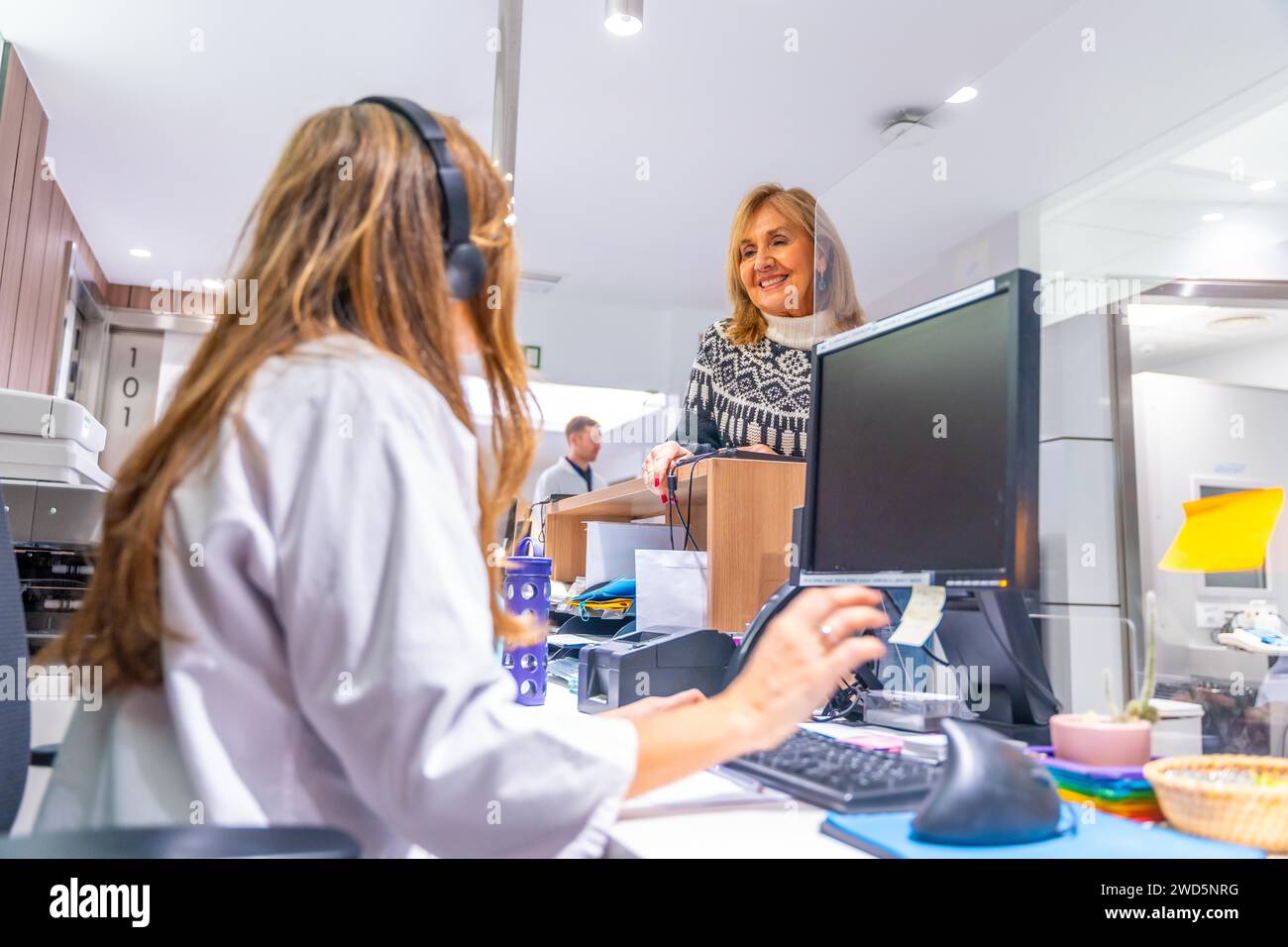 Receptionist of an hospital attending a mature woman standing in front ...
