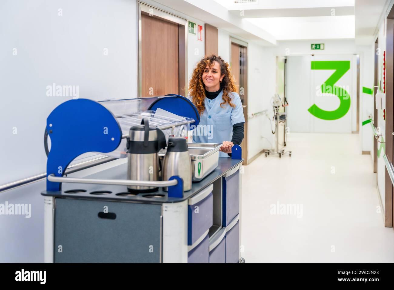 Happy nurse carrying coffee with a trolley along hospital in the ...